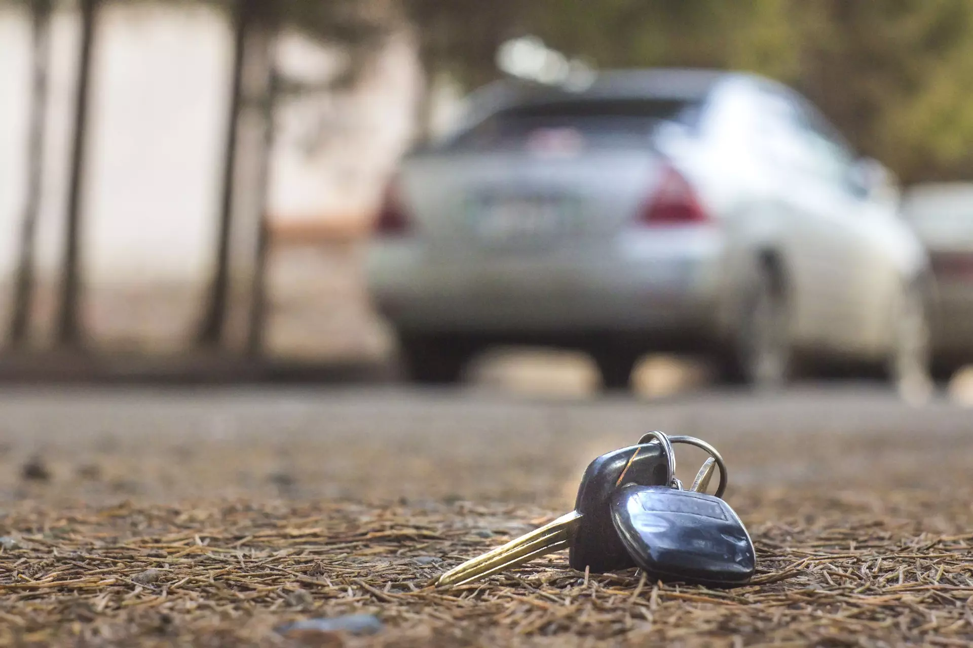 Загублені ключі від автомобіля на землі, на фоні якого стоїть автомобіль (розмитий).
