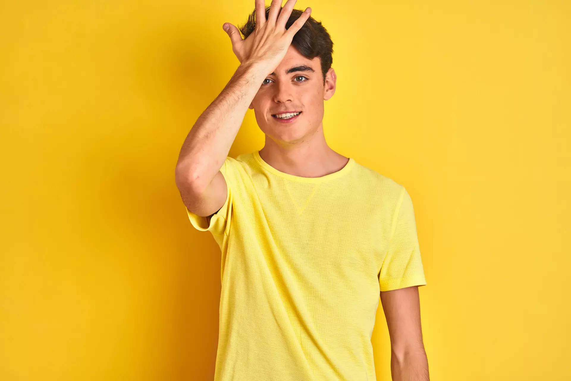 सुनसान पृष्ठभूमि पर पीली टी-शर्ट पहने किशोर लड़के ने गलती से सिर पर हाथ रख लिया, गलती याद आ गई। भूल गए, खराब स्मृति अवधारणा।