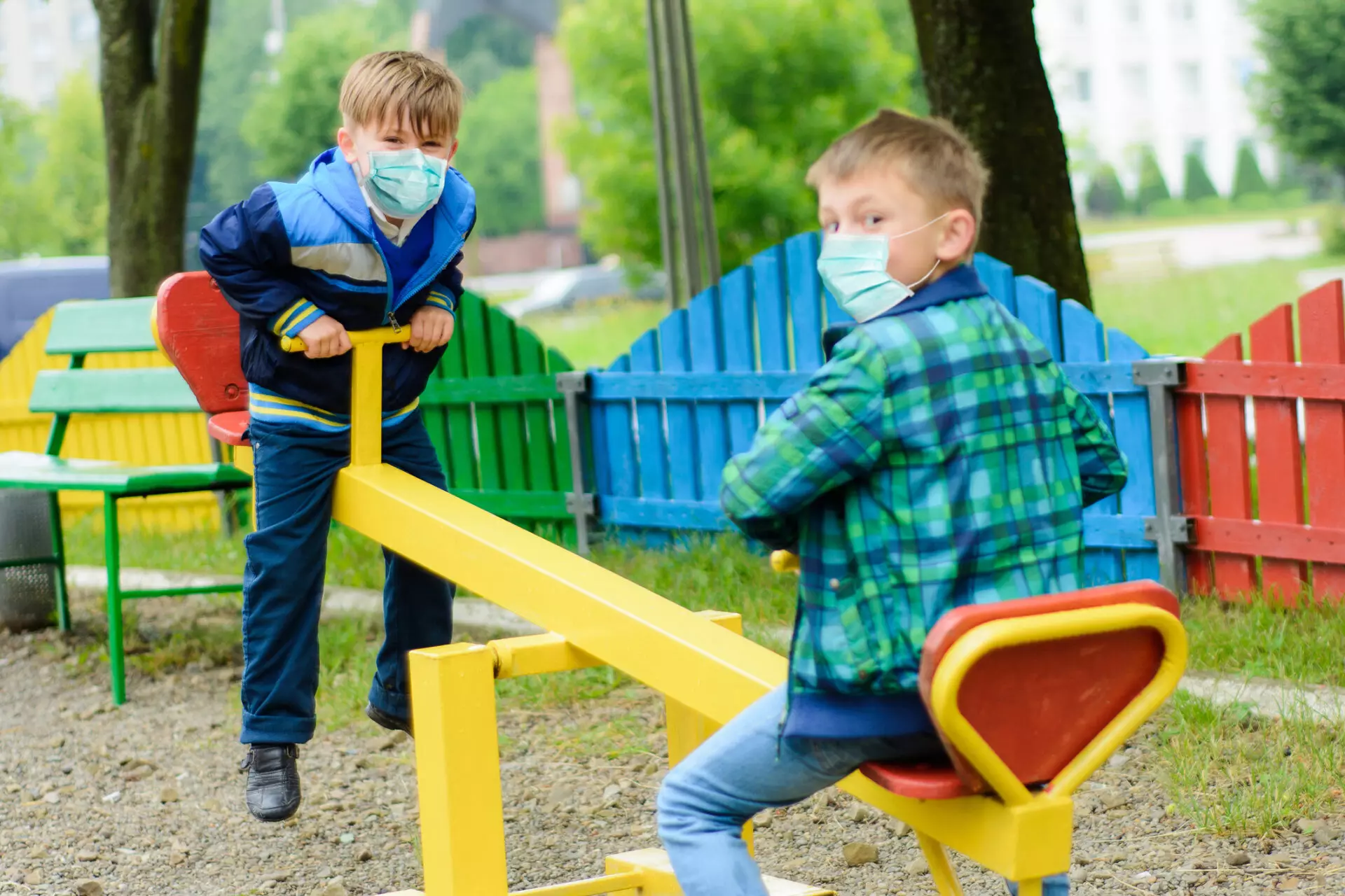 A escola de nenos con máscaras médicas xoga nun parque infantil de corentena durante unha pandemia de coronavirus 2021