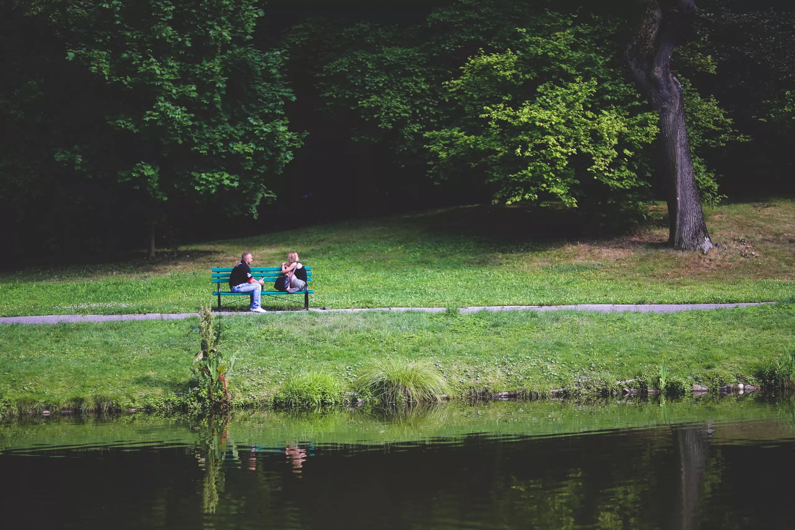 Tată și fiică cu ADHD vorbind pe o bancă într-un parc de lângă lac