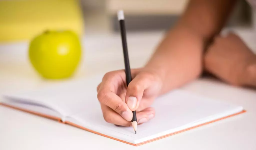 Tyttö, jolla on ADHD, kirjoittaa muistikirjaan ja omena vieressään yrittää valmistautua luokkaan