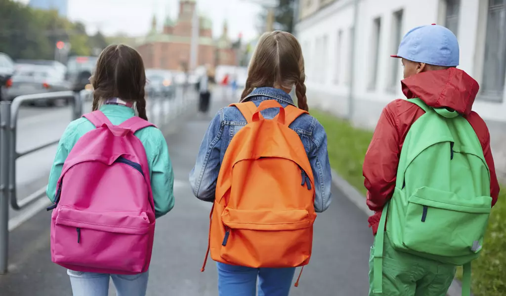 Tre elever med ADHD og fargerike ryggsekker går til skolen i bygate