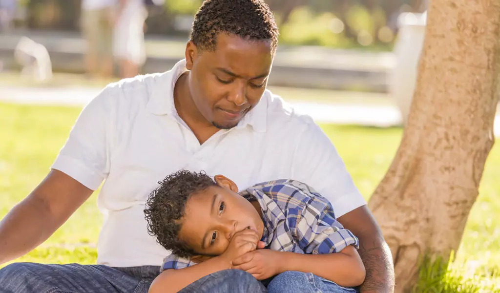 Neno con TDAH apoiado no pai no parque fóra