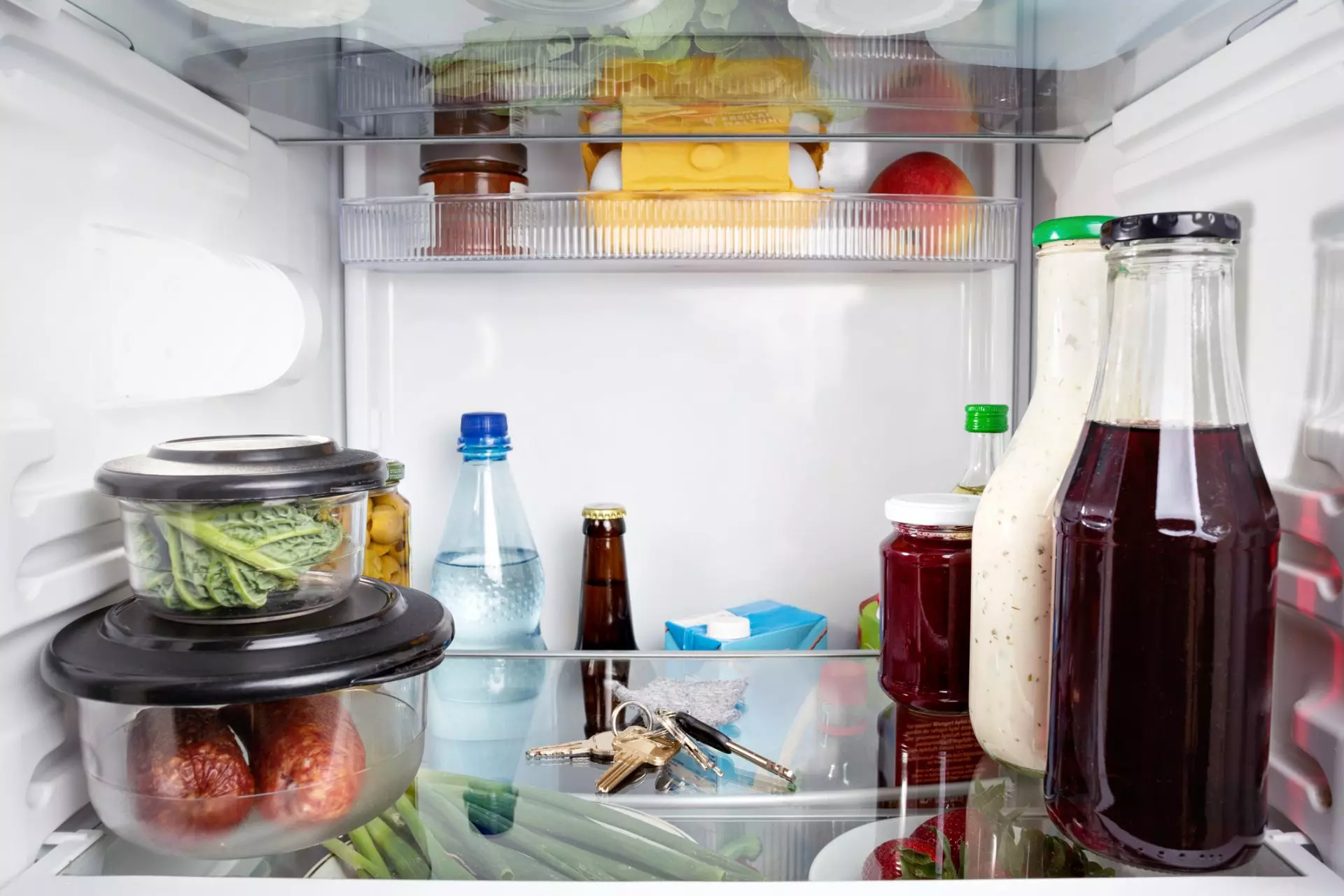 Снимка на вътрешността на хладилник със затворена врата с връзка ключове между хранителни стоки.