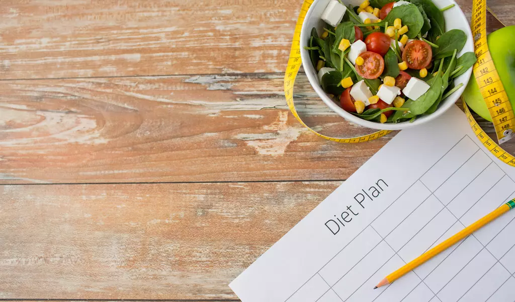 Salātu bļoda ar mērlenti un ābolu uz galda blakus uztura plānam, kas pieder personai ar ADHD