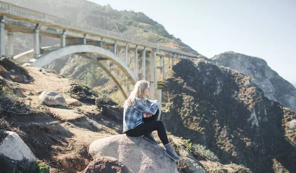 Eine erwachsene Frau mit unaufmerksamem ADHS, die neben einer Brücke sitzt und die Landschaft betrachtet