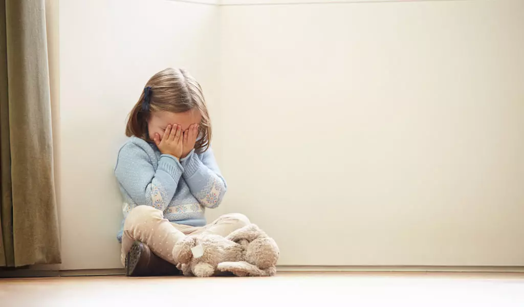 ADHD ունեցող փոքրիկ աղջիկը նստած է անկյունում՝ ձեռքերը դեմքին