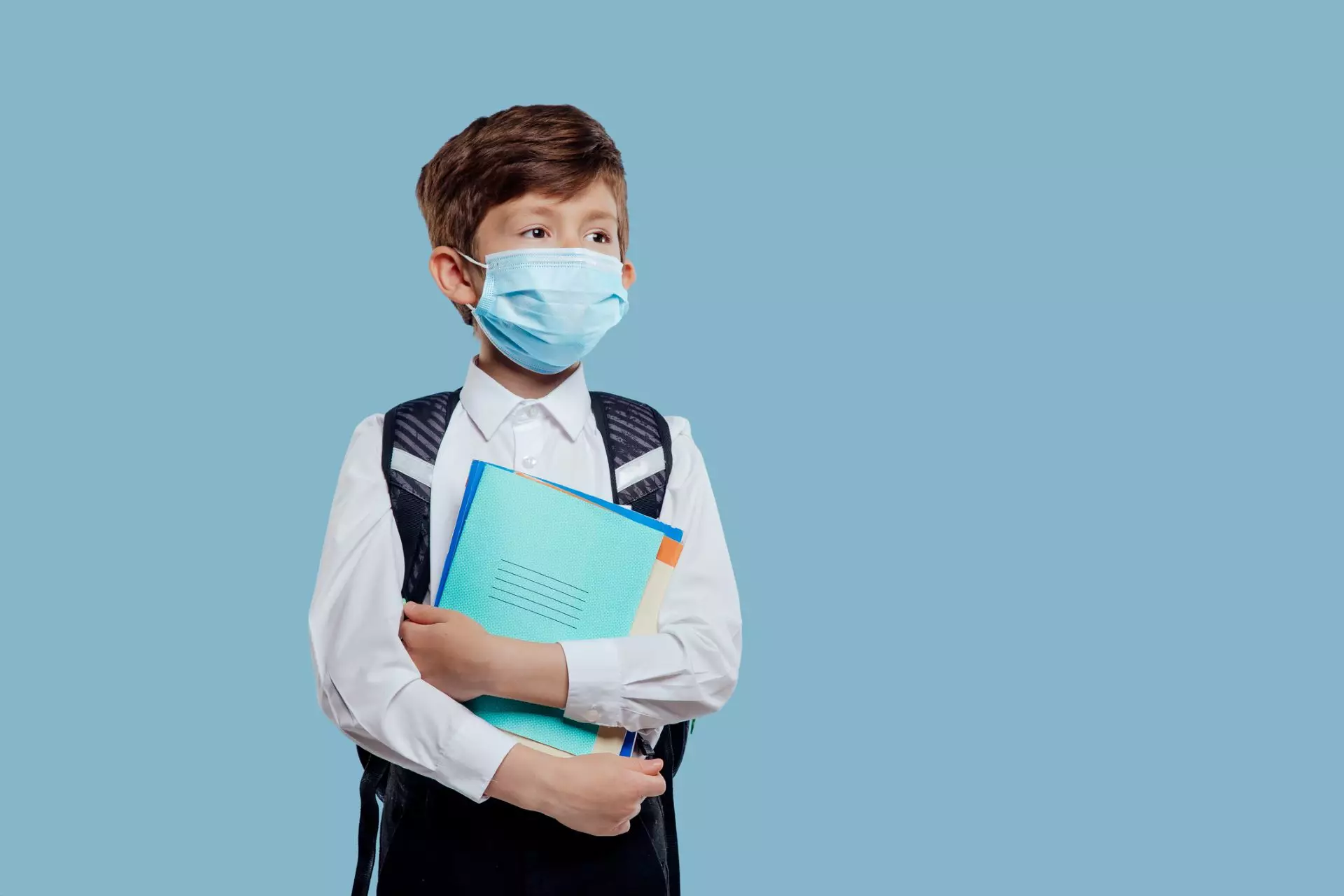 Děti se vracejí do školy - koncept obrazu osamělého dítěte s maskou na obličeji s brašnou a knihami
