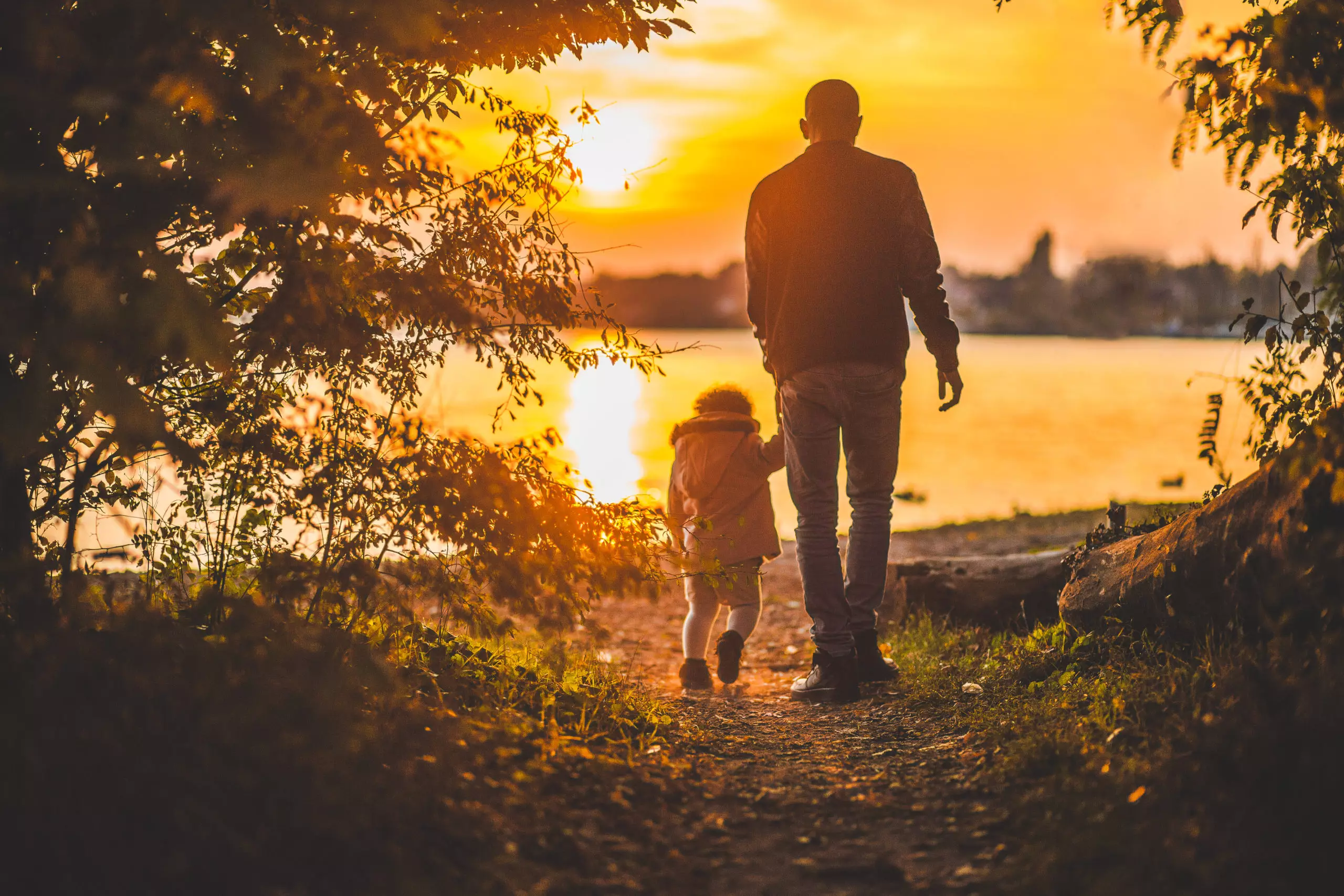 Vientuļš tēvs saulrietā staigā ar ADHD bērnu uz ezeru
