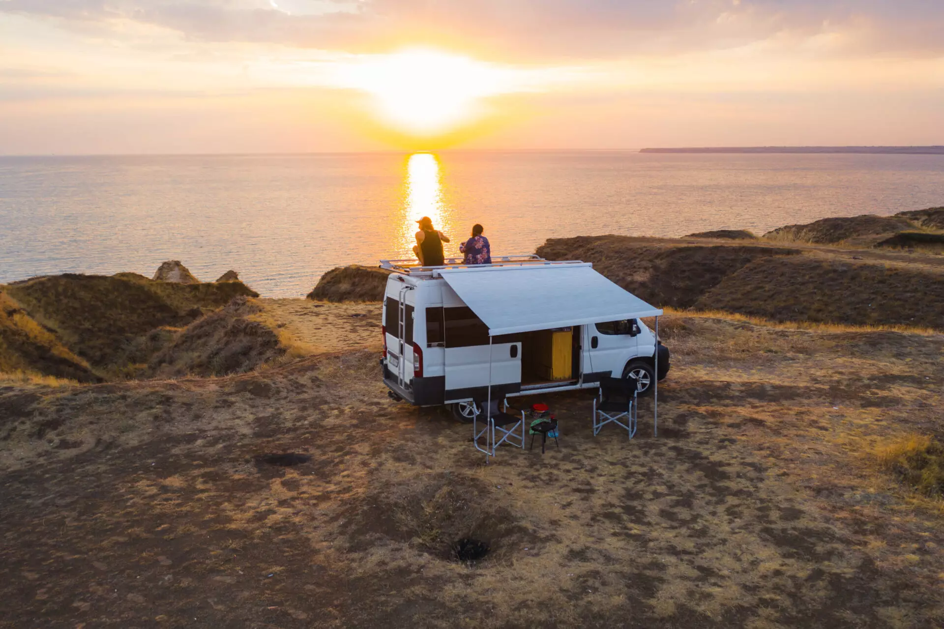 Нар жаргах үед далайн эрэг дээрх кемпийн фургоны дээвэр дээрх хосуудын агаараас харагдах байдал. Oleh_Slobodeniuk/Getty Images