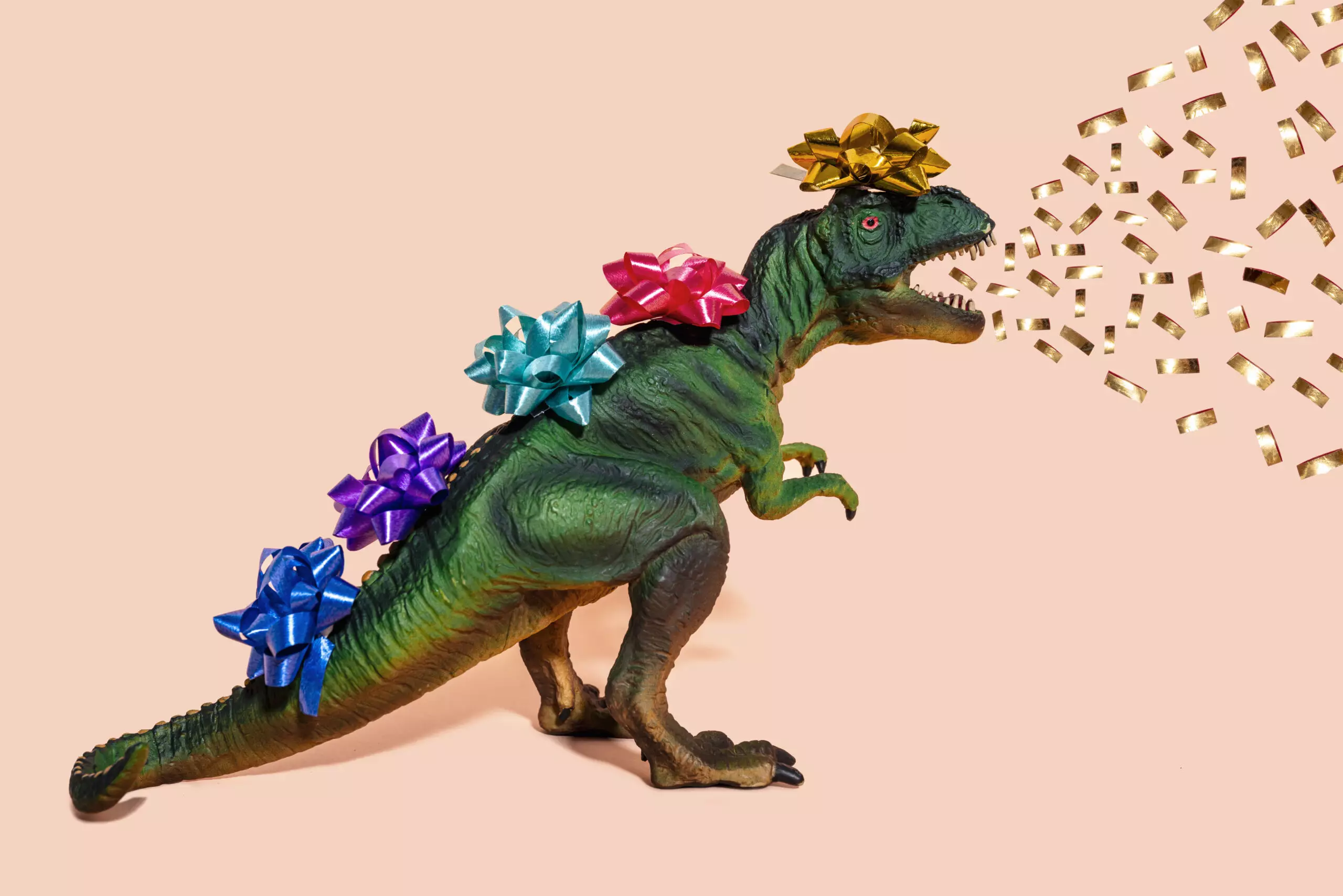 T-Rex dinosaur toy na may mga makukulay na regalong busog na naglalabas ng confetti mula sa kanyang bibig. Volanthevist/Getty Images