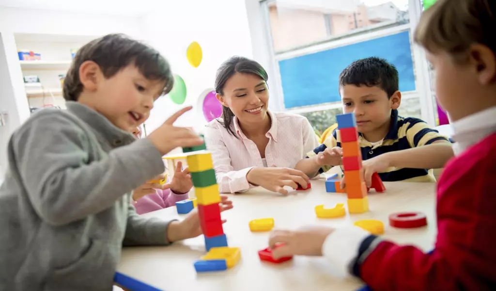 Otroci z ADHD se igrajo s kockami v učilnici, medtem ko jih učitelj opazuje kot del šolskih nastanitev po načrtih IEPS in 504