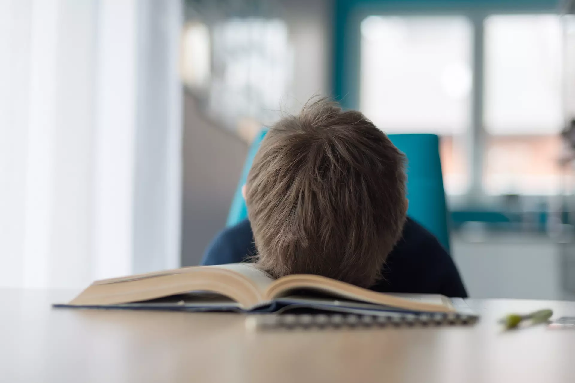ילד עייף בן 8 עושה שיעורי בית ליד השולחן. ילד קורא ספר ליד השולחן.