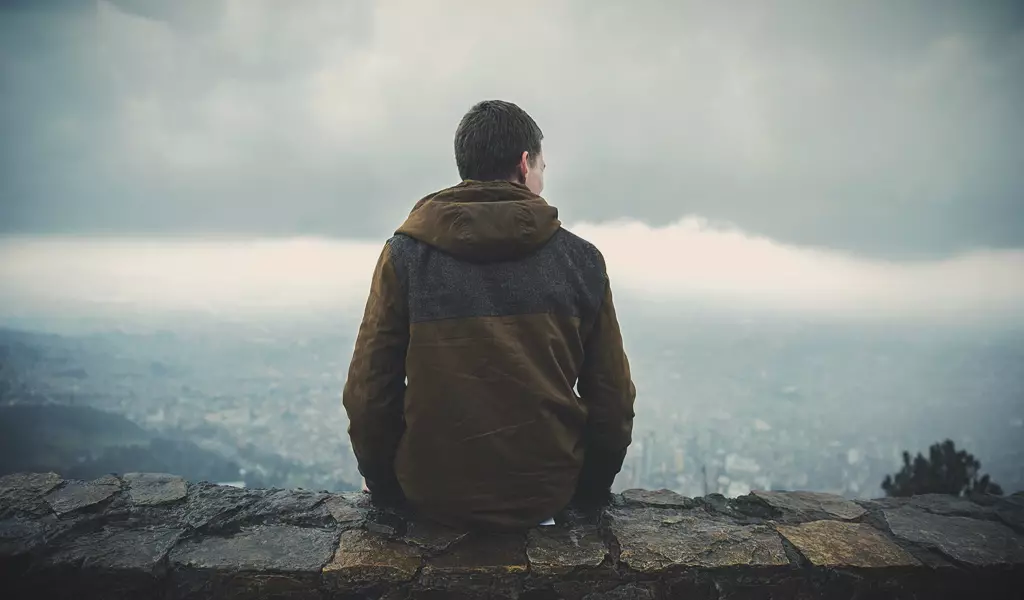Hombre con TDAH y depresión sentado en la cornisa de la pared con vista a la ciudad en un día lluvioso