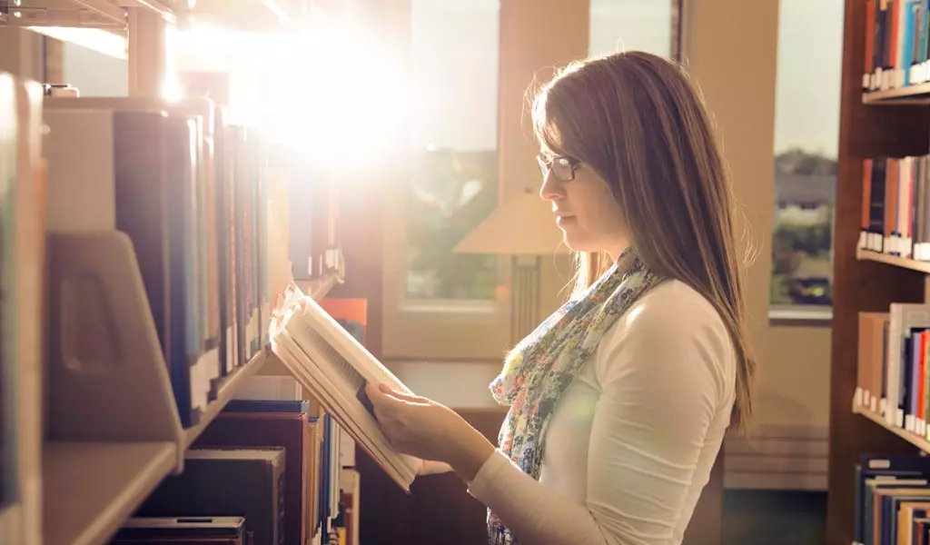 Teenager Meedchen mat ADHD an der Bibliothéik liest Bicher a preparéiert sech op d'Uni