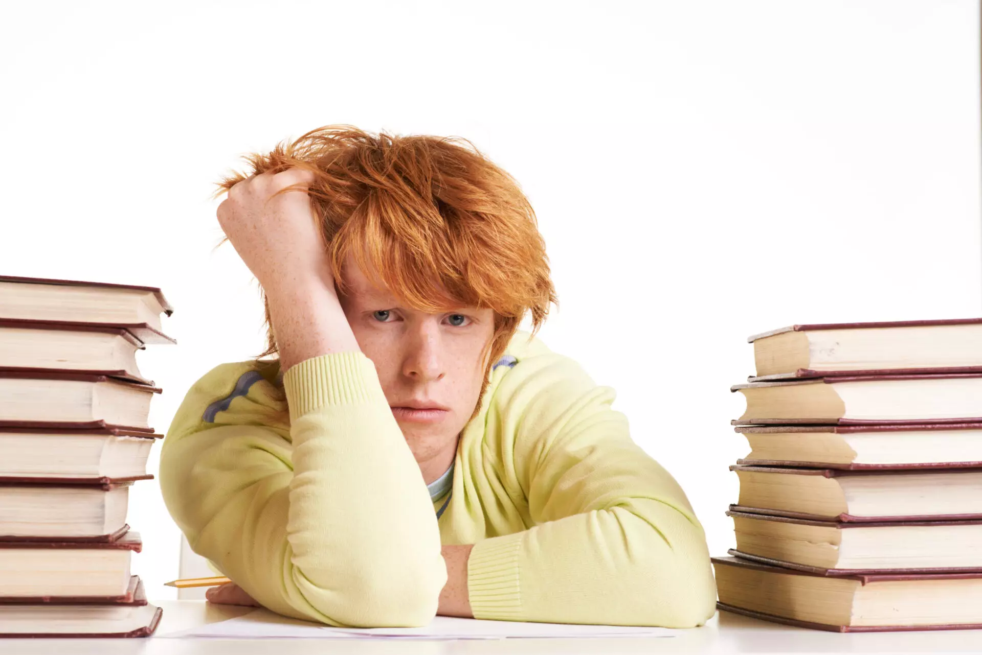 Портрет на црвенокосиот студент кој гледа во камерата помеѓу два купишта книги