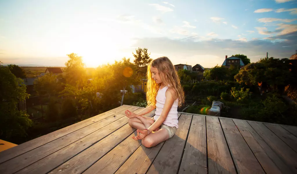 Tyttö, jolla on ADHD, meditoi ulkona kuistilla auringonlaskun aikaan.
