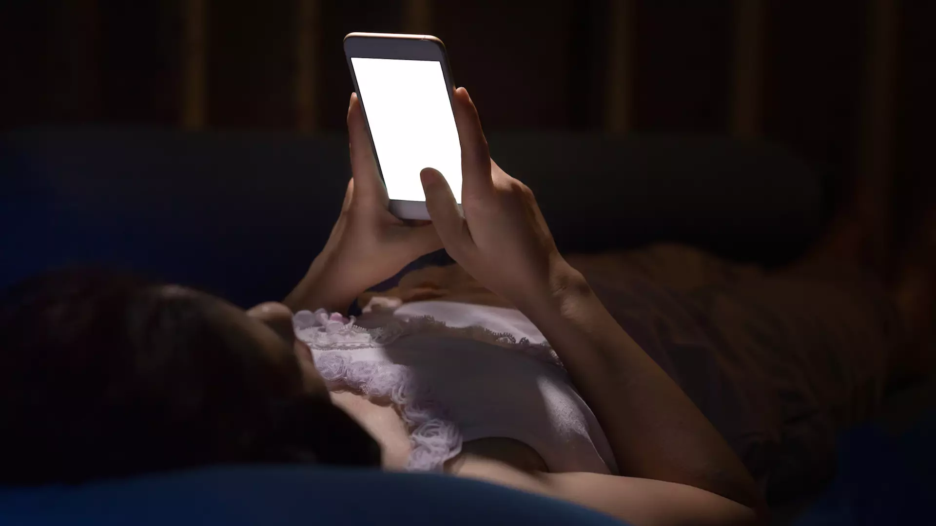 Moteris, kenčianti nuo nemigos, naudojasi mobiliuoju telefonu lovoje, tamsiame tyliame miegamajame