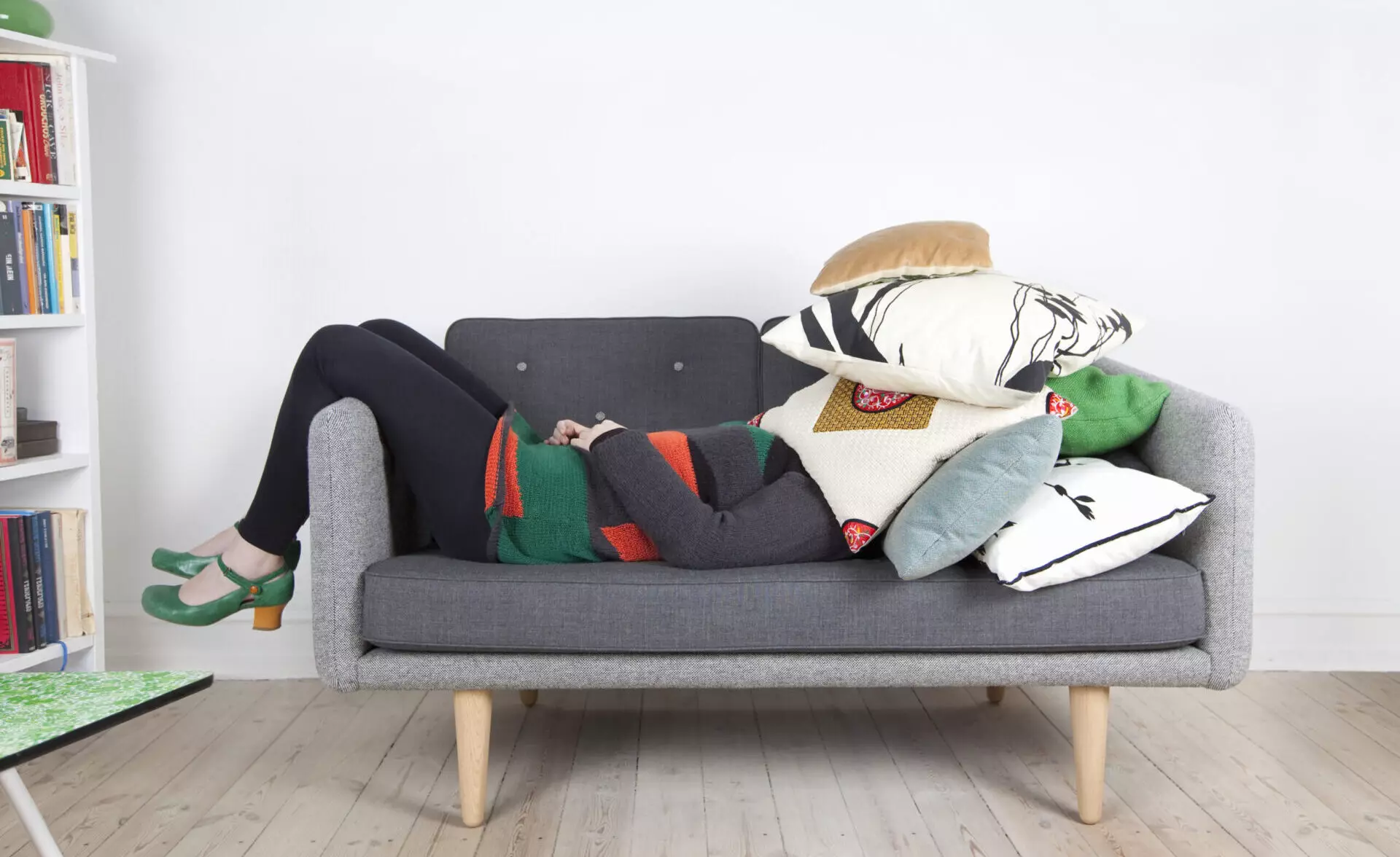 Žena leži na sofi s hrpom jastuka preko glave.