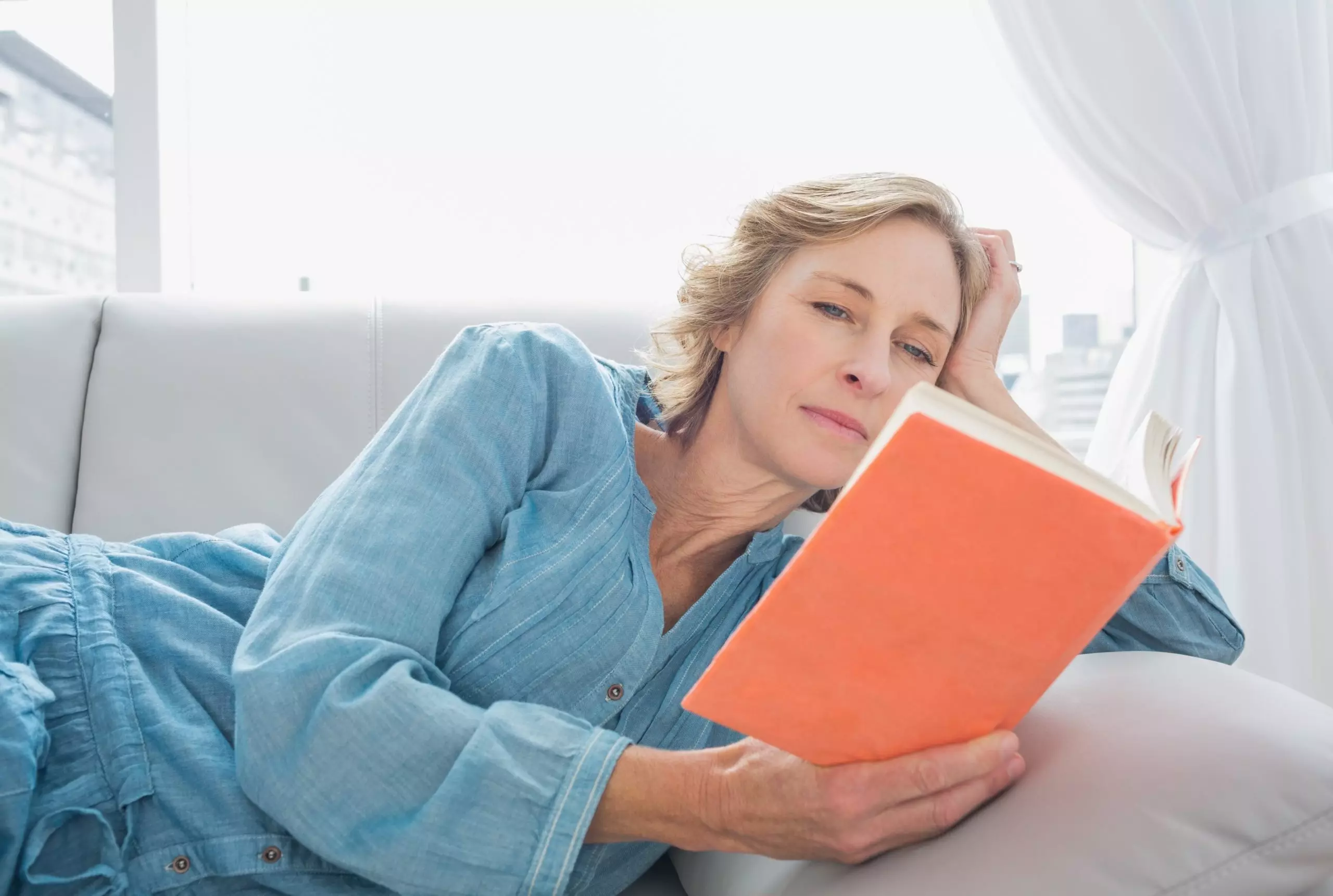 Een vrouw met ADHD ontspant en leest een boek op de bank, terwijl ze wat persoonlijke tijd neemt in haar huwelijk.