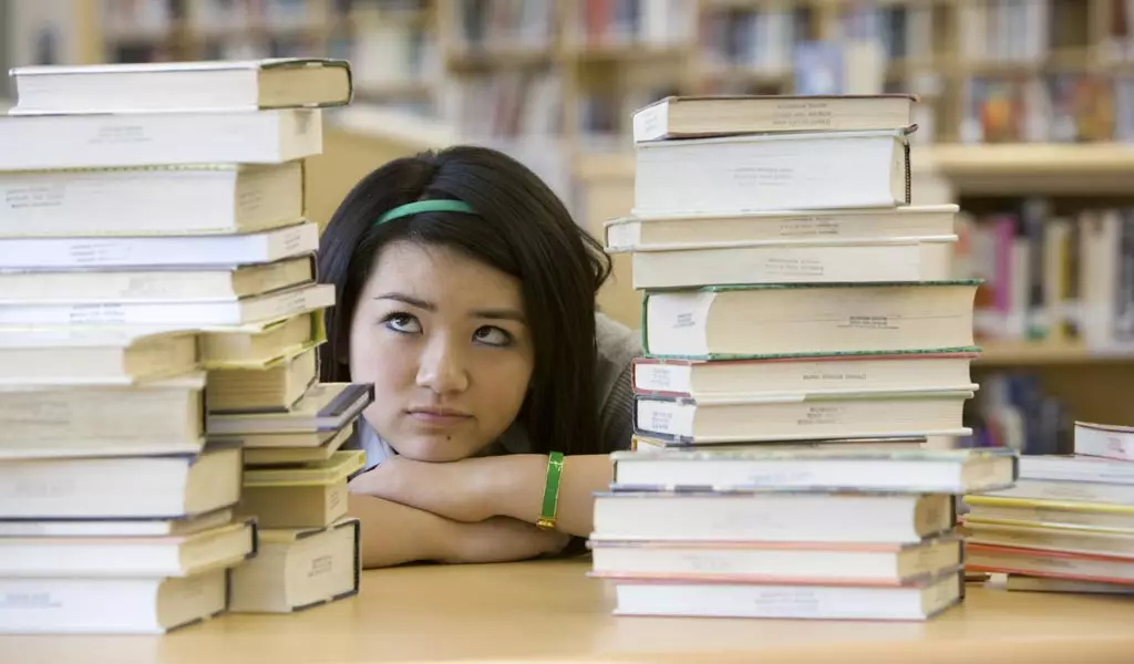 Học sinh trung học mắc chứng ADHD trong thư viện nhìn chằm chằm vào chồng sách chuẩn bị vào đại học