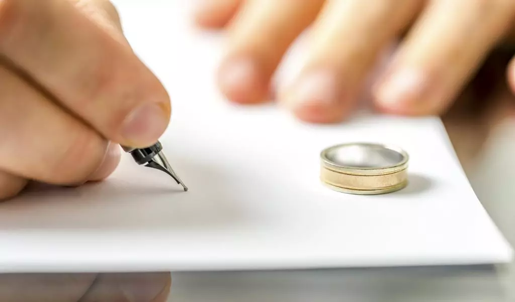 Primo piano della mano di una persona con ADHD che firma i documenti di divorzio con l'anello nelle vicinanze