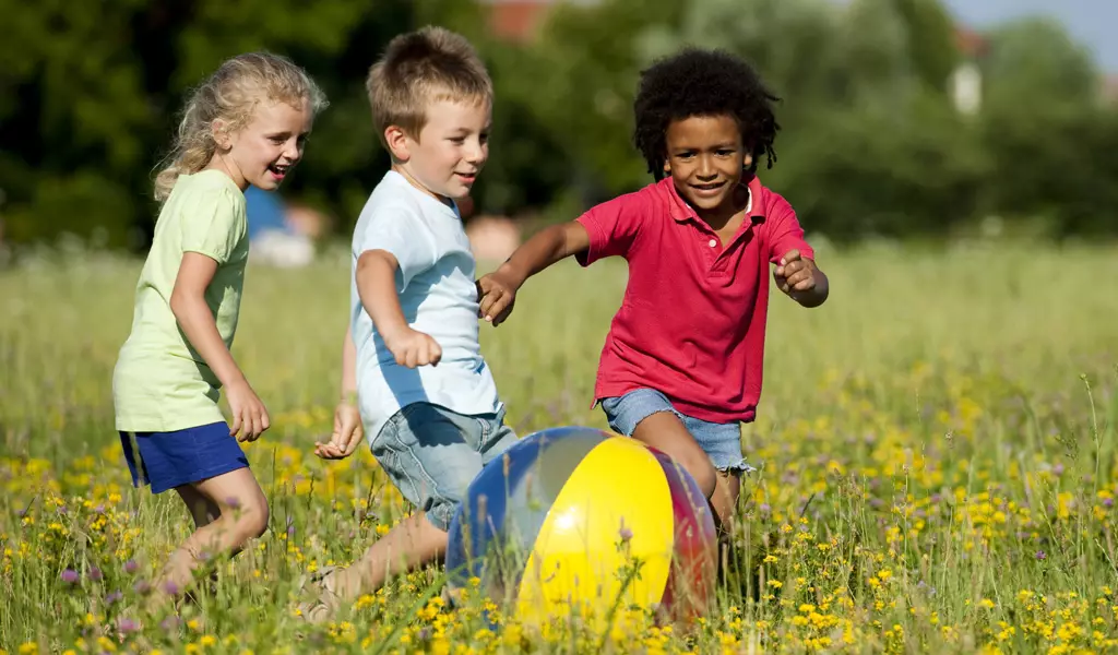 Tres nenos con TDAH xogando cunha pelota de praia no campo exterior, ben portados grazas a un novo medicamento para o TDAH