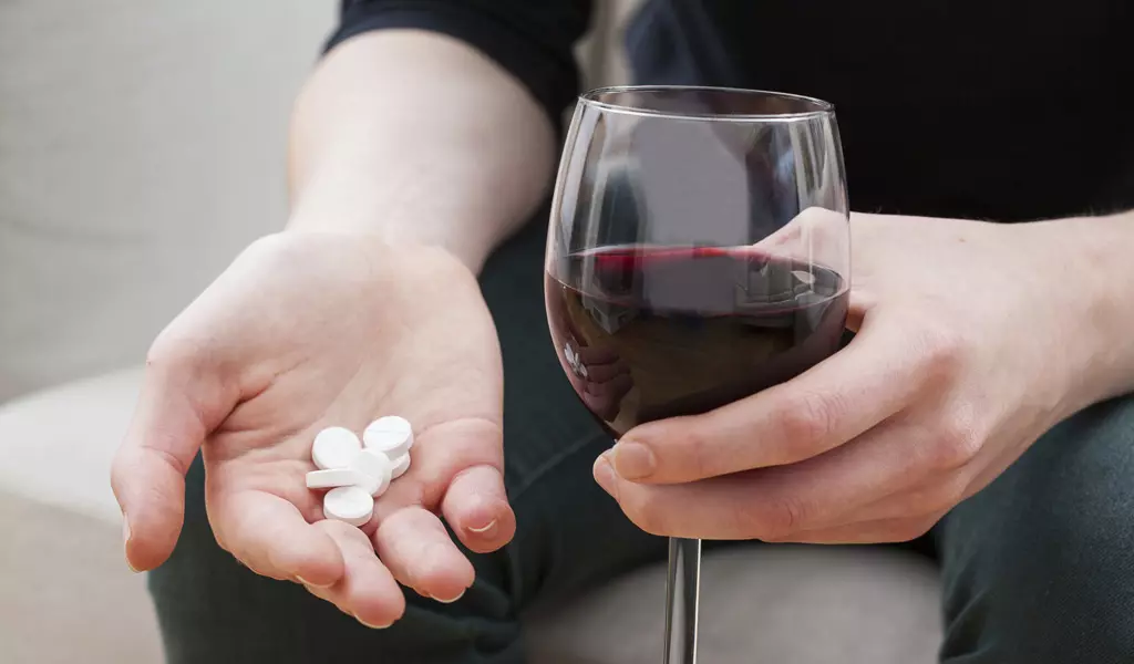 Pria dengan ADHD memegang obat di satu tangan dan segelas anggur di tangan lainnya