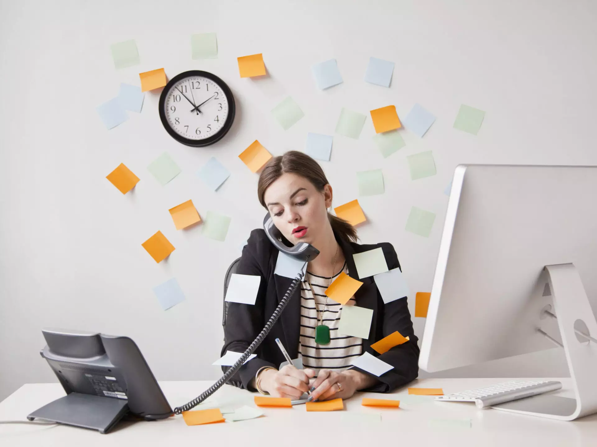 Foto de estudio de una joven que trabaja en la oficina cubierta con notas adhesivas. Imágenes de Jessica Peterson/Getty.