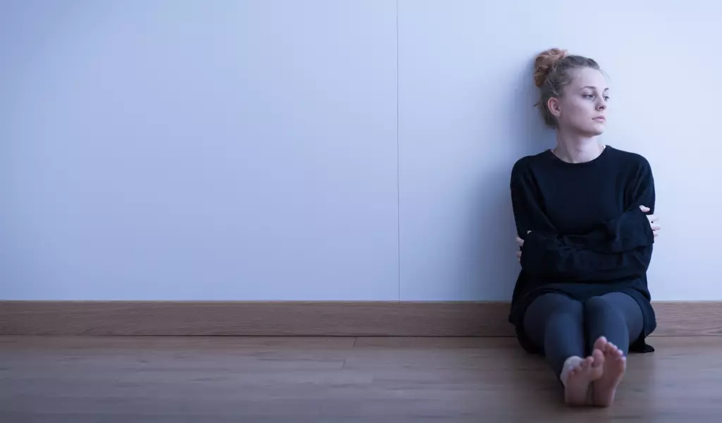 Djevojka s ADHD-om i depresijom sjedi na podu uz zid