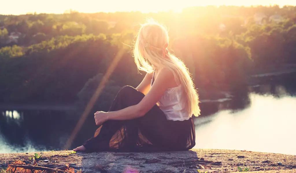 Žena s ADHD-om sjedi na vrhu planine s pogledom na jezero u zalazak sunca i razmišlja o svojoj dijagnozi