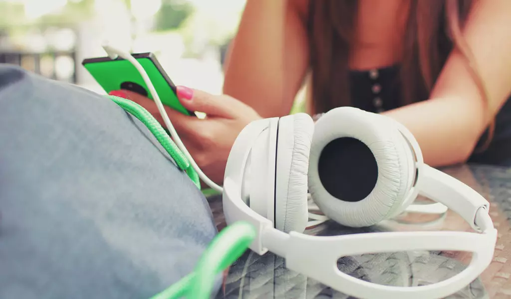Tinejdžerica s ADHD-om igra se na pametnom telefonu sa slušalicama i torbom na stolu vani