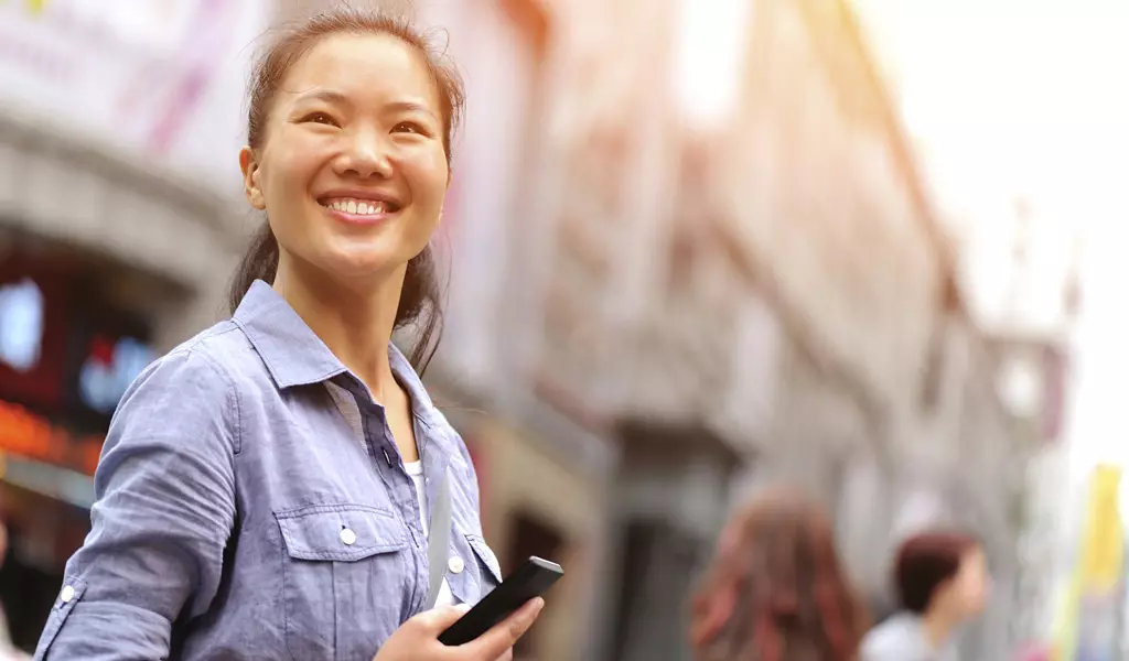 Wanita dengan ADHD, di jalan kota, tersenyum dan memegang ponsel setelah menggunakan aplikasi daftar tugas untuk organisasi