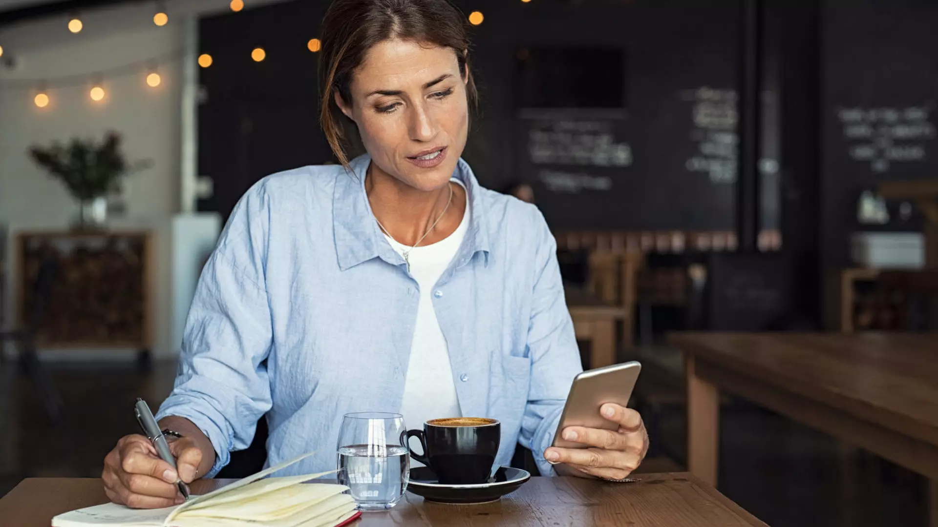 Зряла жена седи в кафене на маса и пише съобщение на смартфон. Блогър на средна възраст, който прави бележки с помощта на приложение за организиране на телефона. Бизнесдама чете информация от смартфон, докато работи дистанционно в интериора на кафене.
