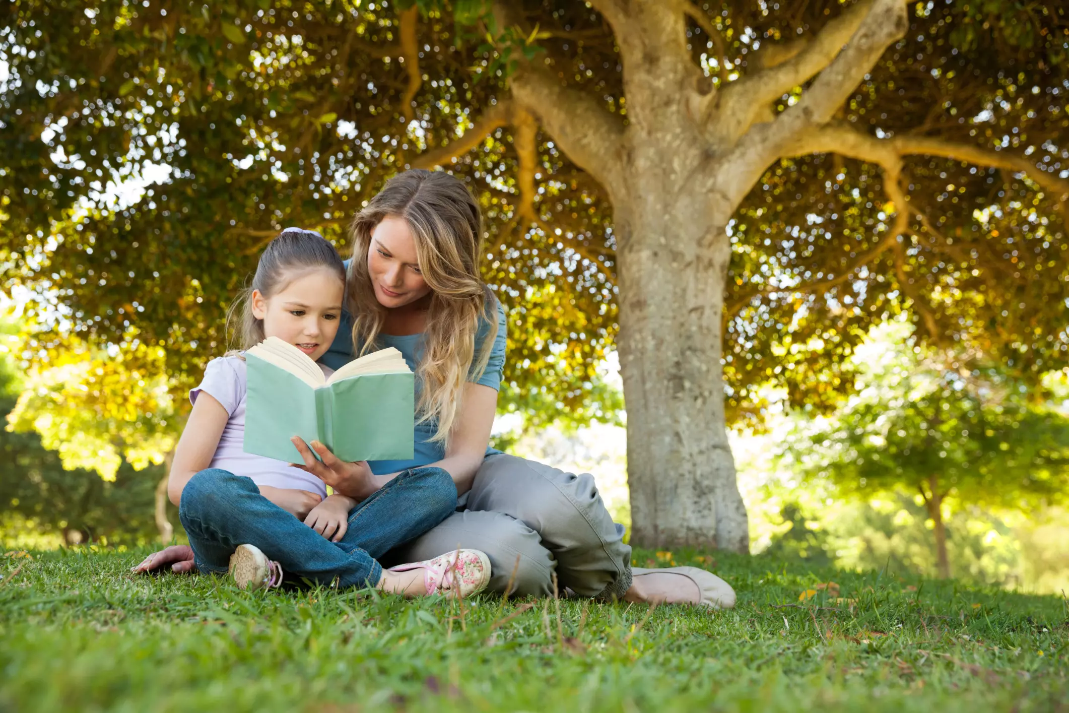 დედა და ქალიშვილი ავითარებენ აკადემიურ უნარებს ზაფხულში ხის ქვეშ წიგნის კითხვით
