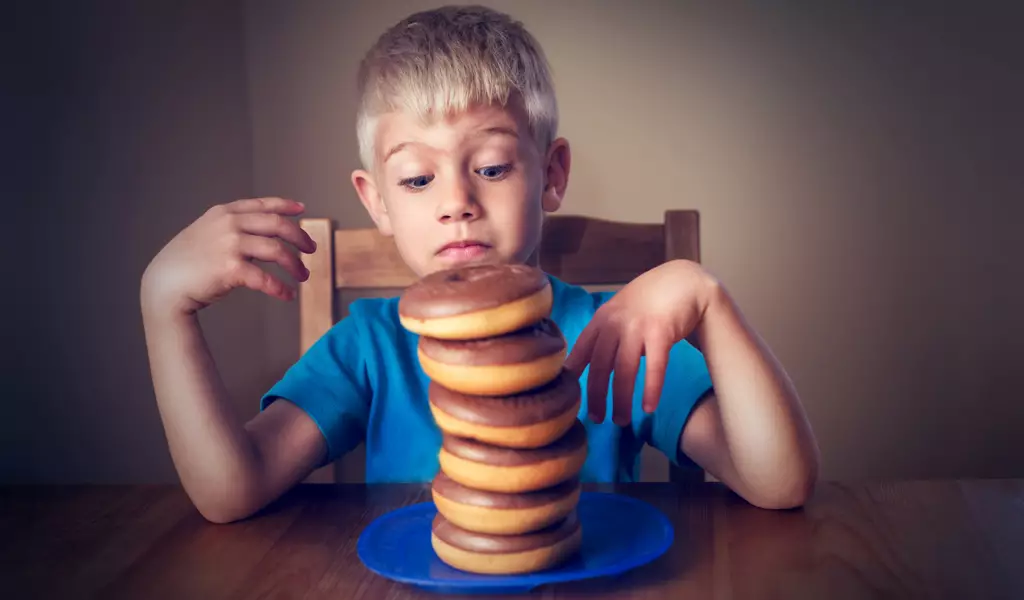 Een jongen met ADHD, starend naar een grote stapel donuts met suiker