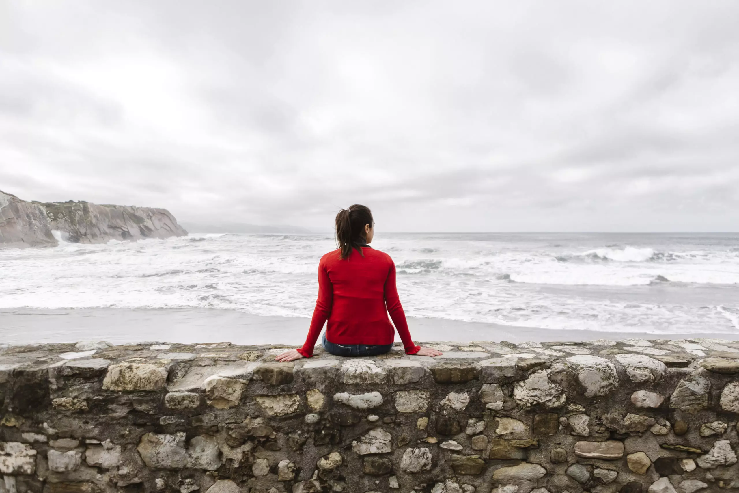 Playa de Itzurun, Zumaia, Euskadi, Hispaania – tagantvaade lõdvestunud naisest, kes vaatab pilves päeval merd. Westend61 / Getty Images
