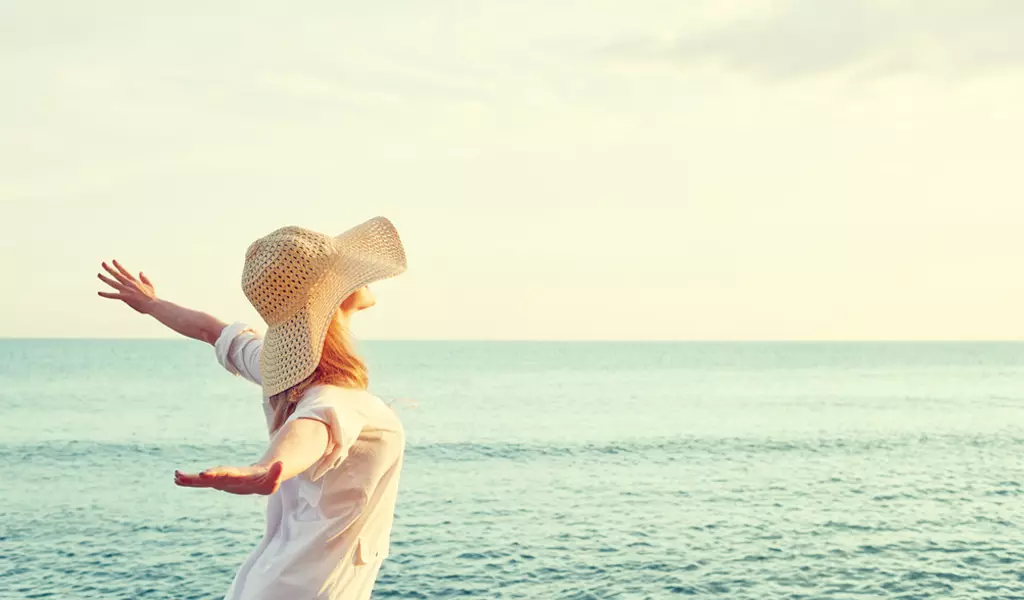 ADHD-ga naine, kes seisab ookeani ääres ja kannab mütsi, sirutab käed laiali ja embab oma hilise ADHD diagnoosi