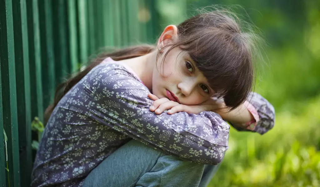 Unha moza que trata de desatención con TDAH, sentada coa cabeza sobre os xeonllos