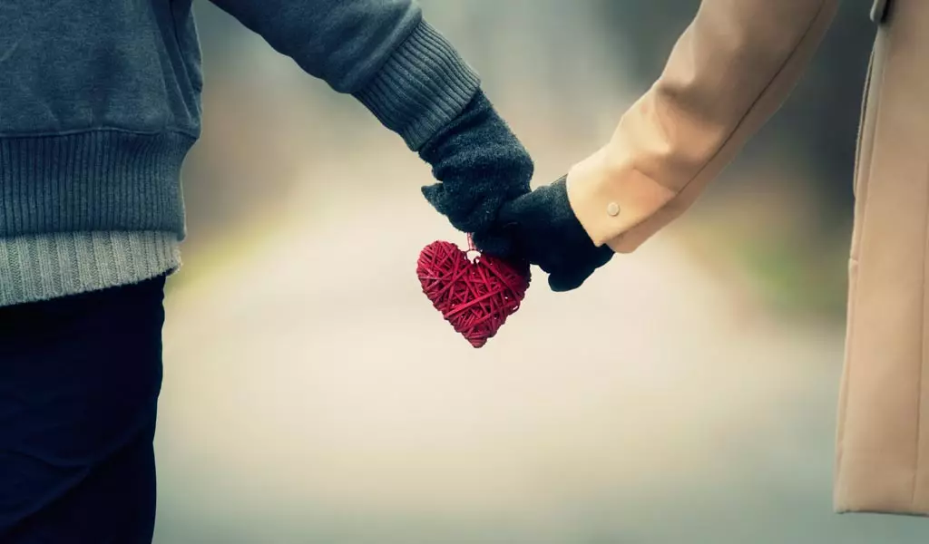 Poročeni par z ADHD se na sprehodu drži za roke z okraskom v obliki srca med njima