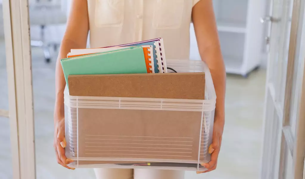 Γυναίκα με ΔΕΠΥ που κουβαλά κουτί με πράγματα εκτός γραφείου μετά την απόλυσή του