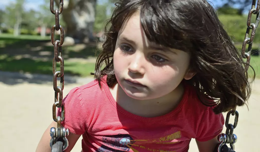 Ledsen tjej med sensorisk bearbetningsstörning och ADHD på gungan i parken