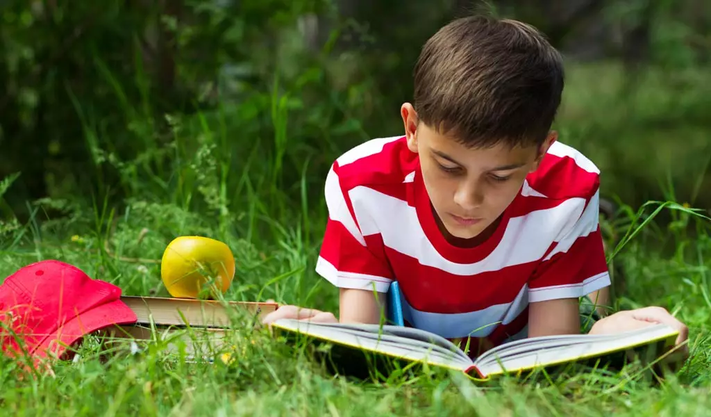 صبي مراهق مصاب باضطراب فرط الحركة ونقص الانتباه يقرأ كتابًا في العشب