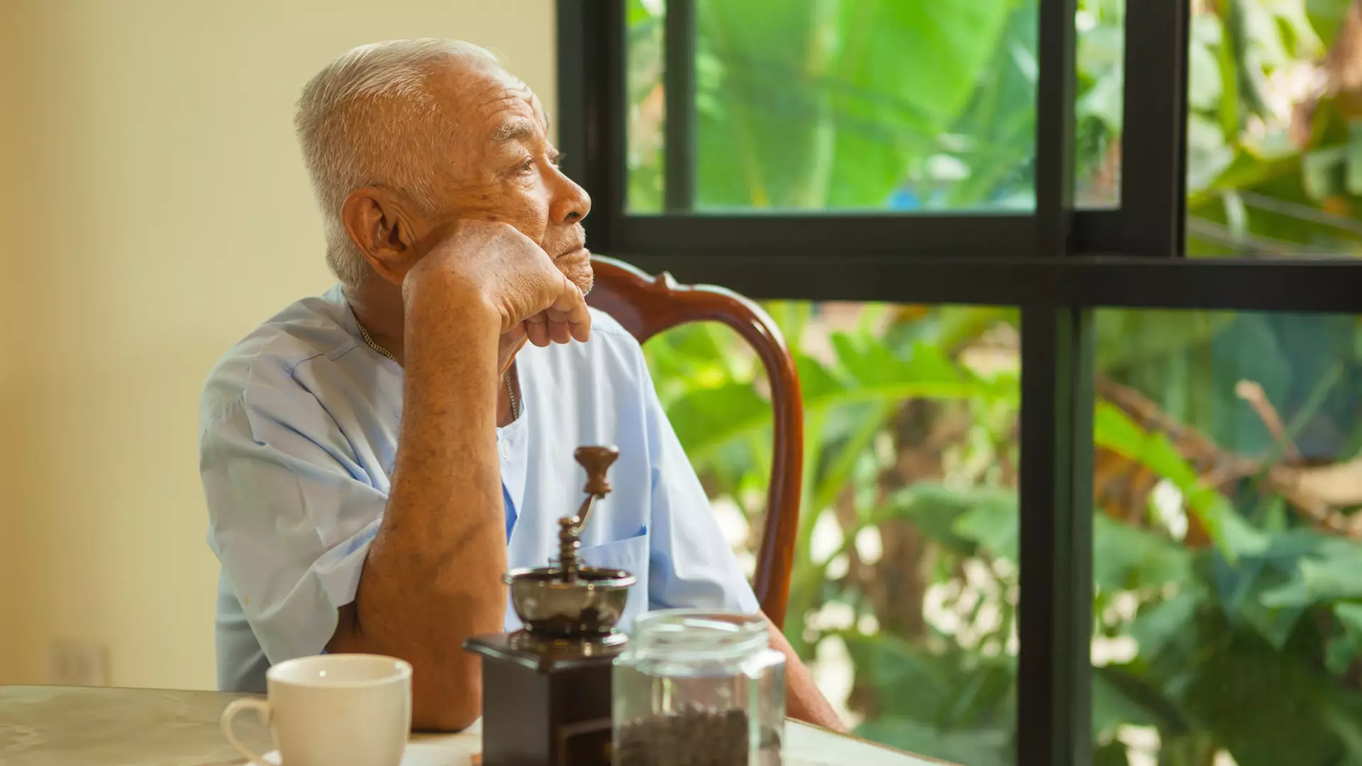 Пожилой мужчина с СДВГ тихо смотрит в окно своего дома.