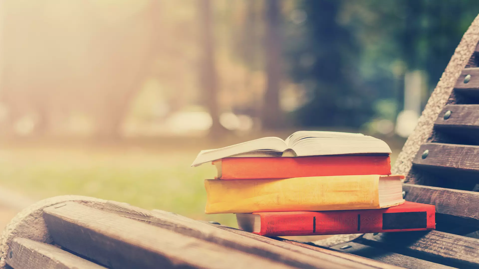 Sommarplaner: Hög med inbundna böcker och öppen bok liggandes på bänken
