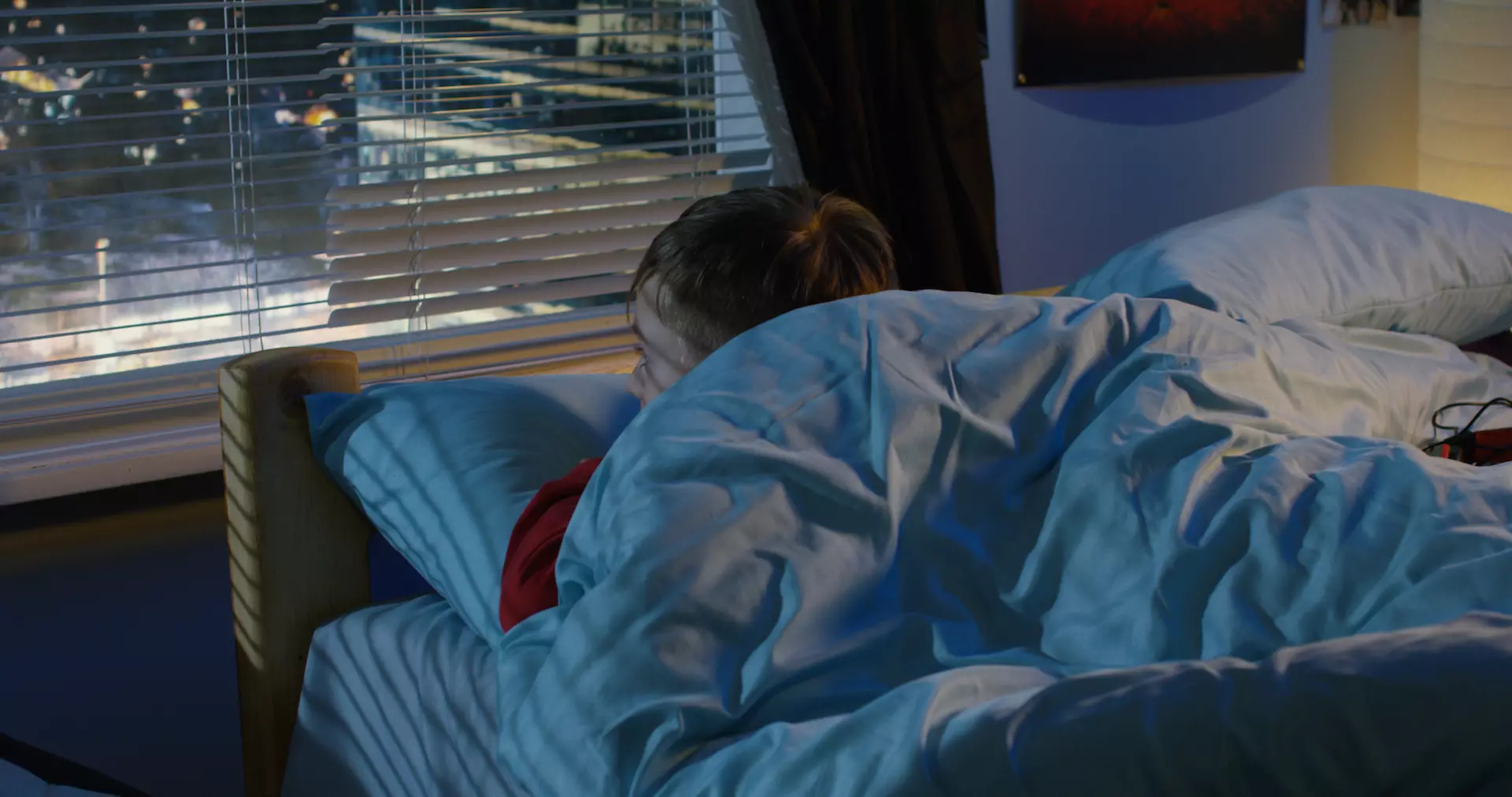 Shot vanuit een gemiddeld perspectief van een jongen die uit het raam kijkt terwijl hij in bed ligt en probeert in slaap te vallen
