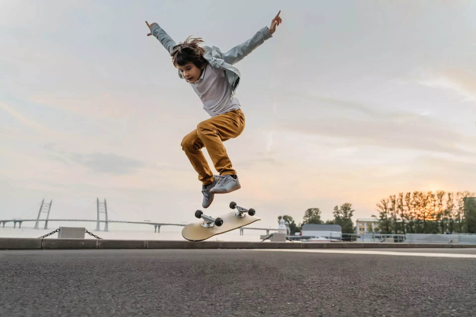 Seun spring op skaatsplank by die straat. Snaakse kindskaatser oefen Ollie op skaatsplank teen sonsondergang.