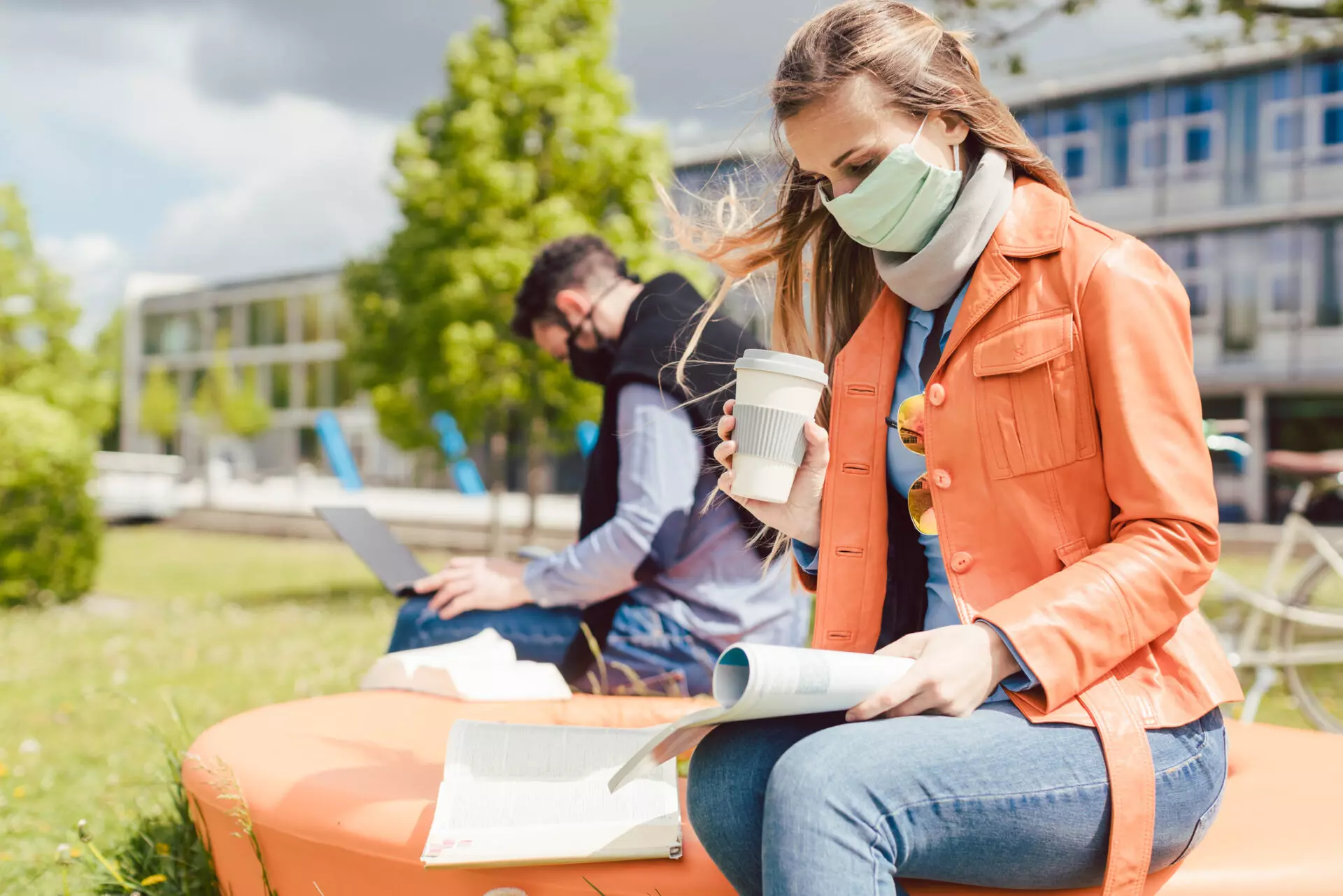 Студентка на универзитетски кампус учи носејќи маска за лице додека работи на својот лаптоп