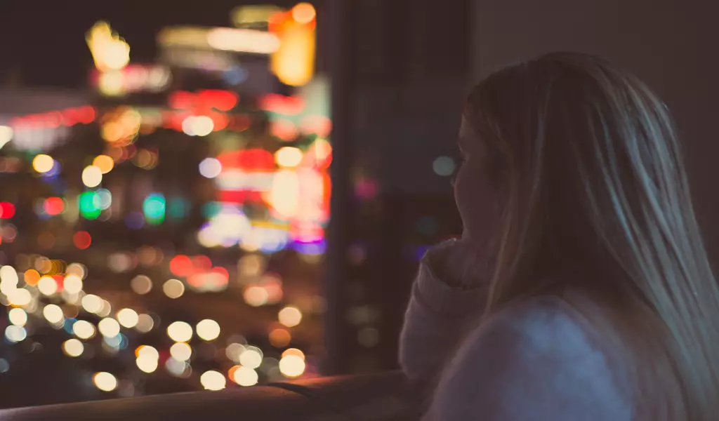 La ragazza con ADHD e depressione guarda fuori dall'appartamento sulla strada della città di notte