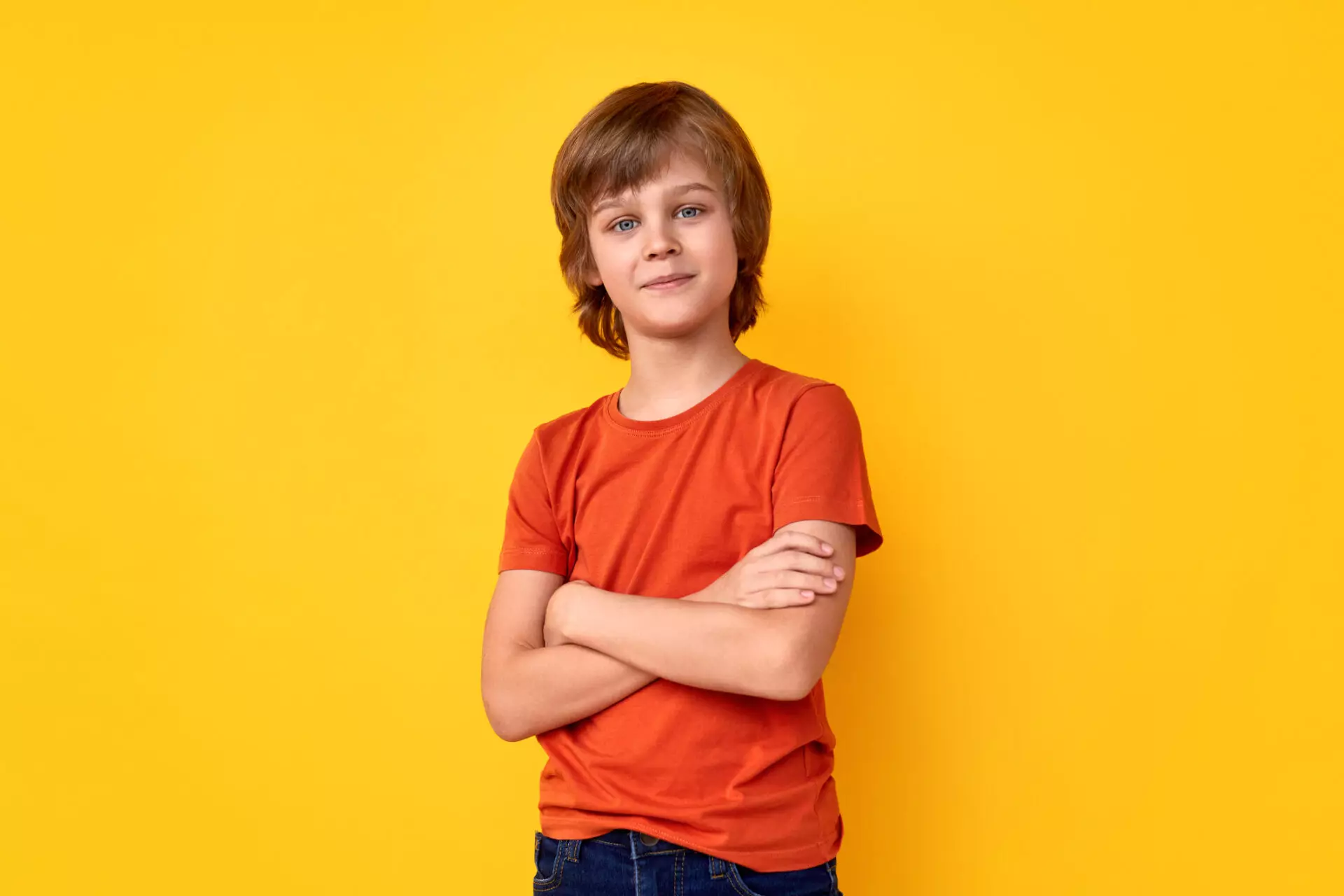 Pozitiven prednajstniški deček v priložnostni obleki drži prekrižane roke in gleda v kamero na živo rumenem ozadju